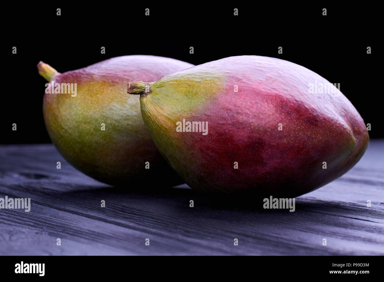 Close up fresh whole mangoes. Two tropical mango fruits on black wooden ...