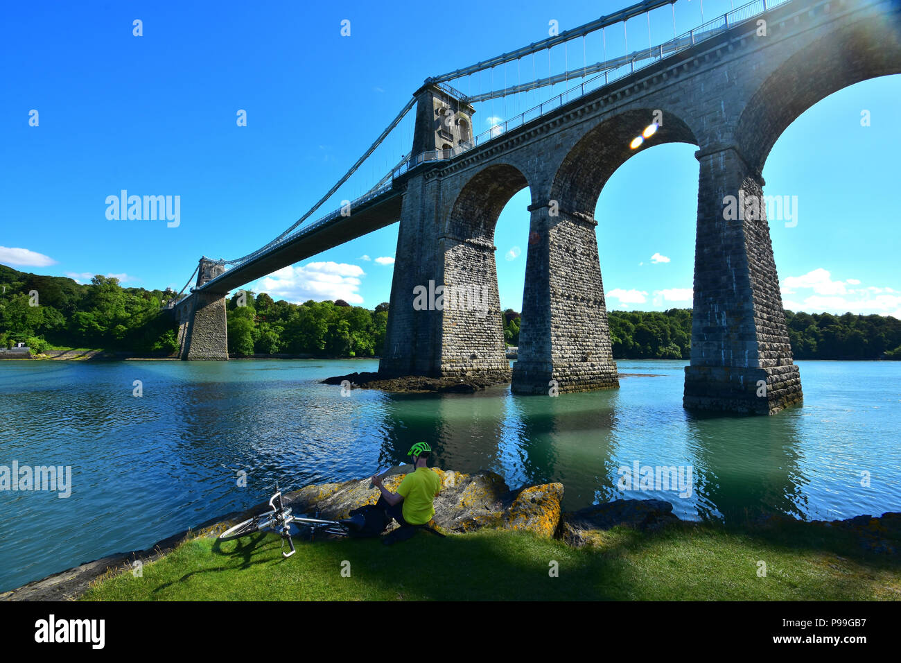 Cyclist reading a map below the Menai Bridge spanning the Menai Strait ...