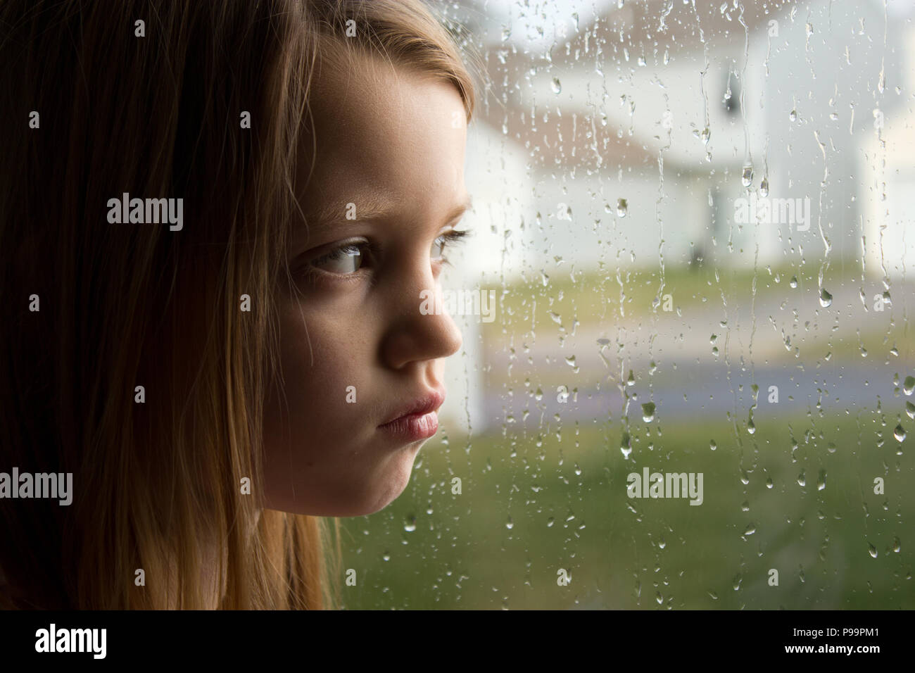 Sad little girl staring out rainy window Stock Photo - Alamy