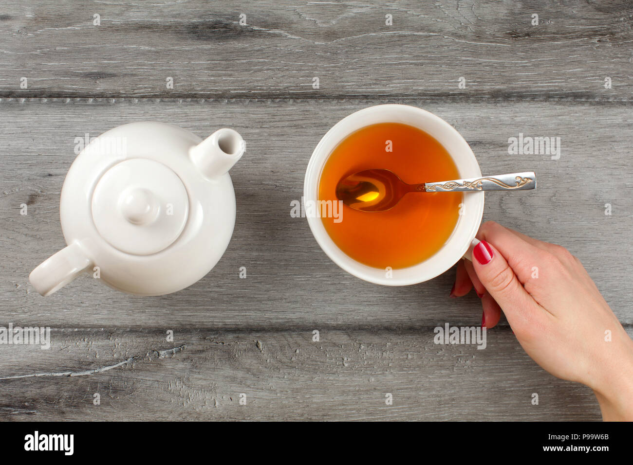 Top view, young woman hand with red nail holding cup of amber tea, with ...