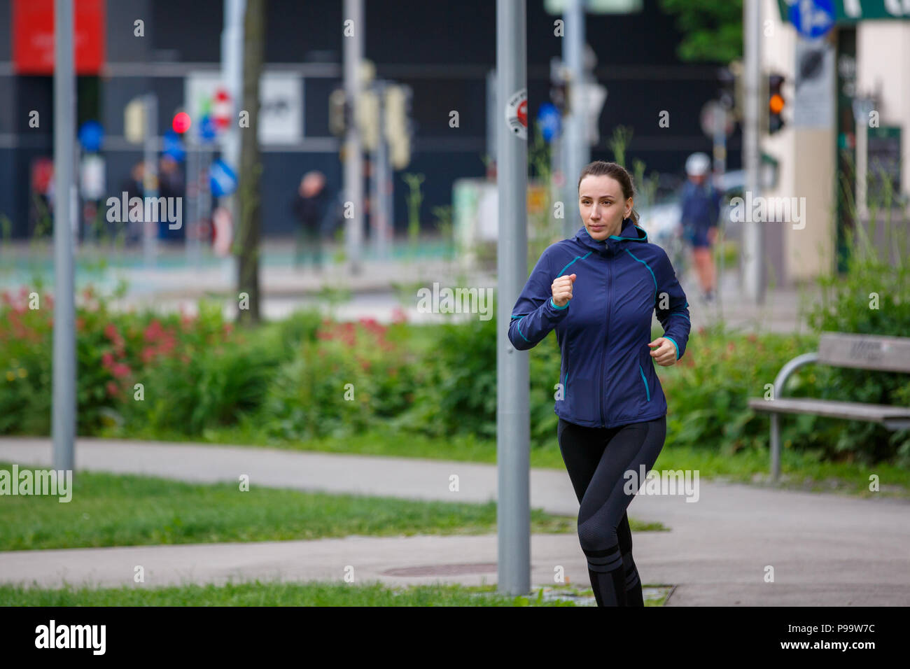 Young woman in blue jacket jogging in park Stock Photo - Alamy