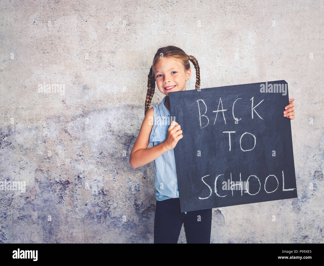 schoolgirl is holding blackboard with the words back to school in front ...