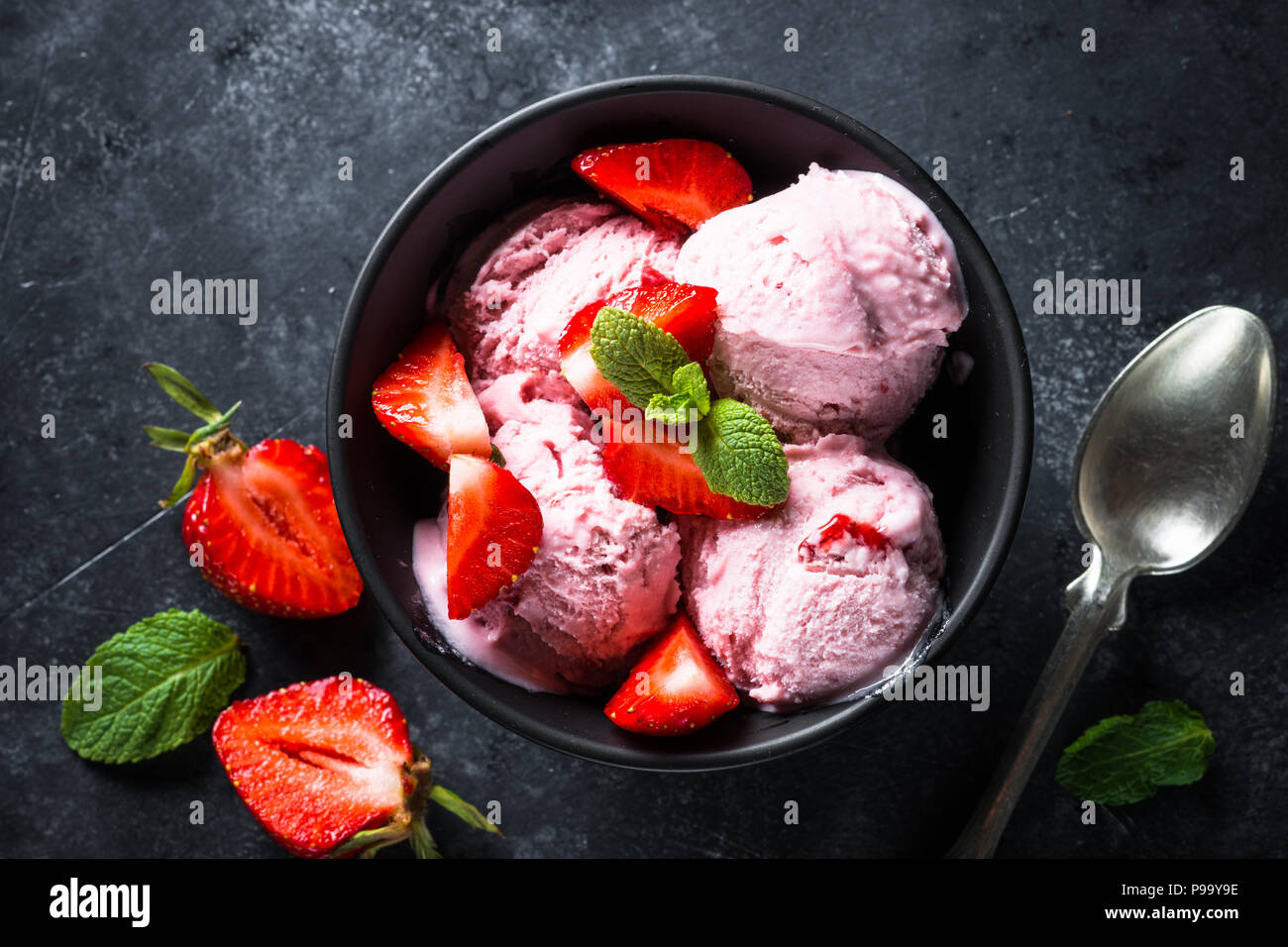 Strawberry ice cream with fresh berries in a bowl on black. Top view ...