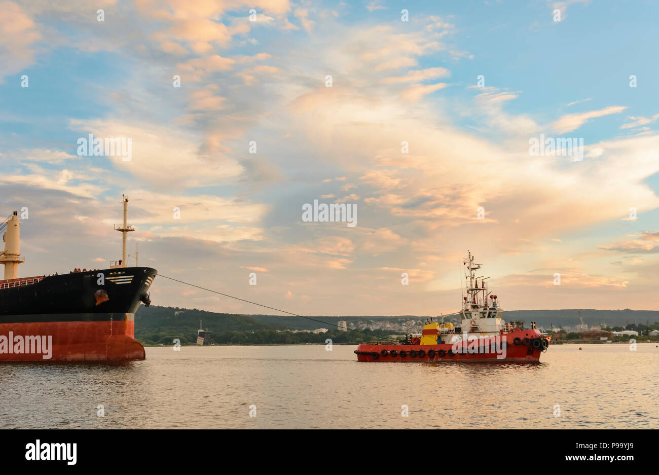 Tug boat entering the harbor with big cargo boat Stock Photo - Alamy