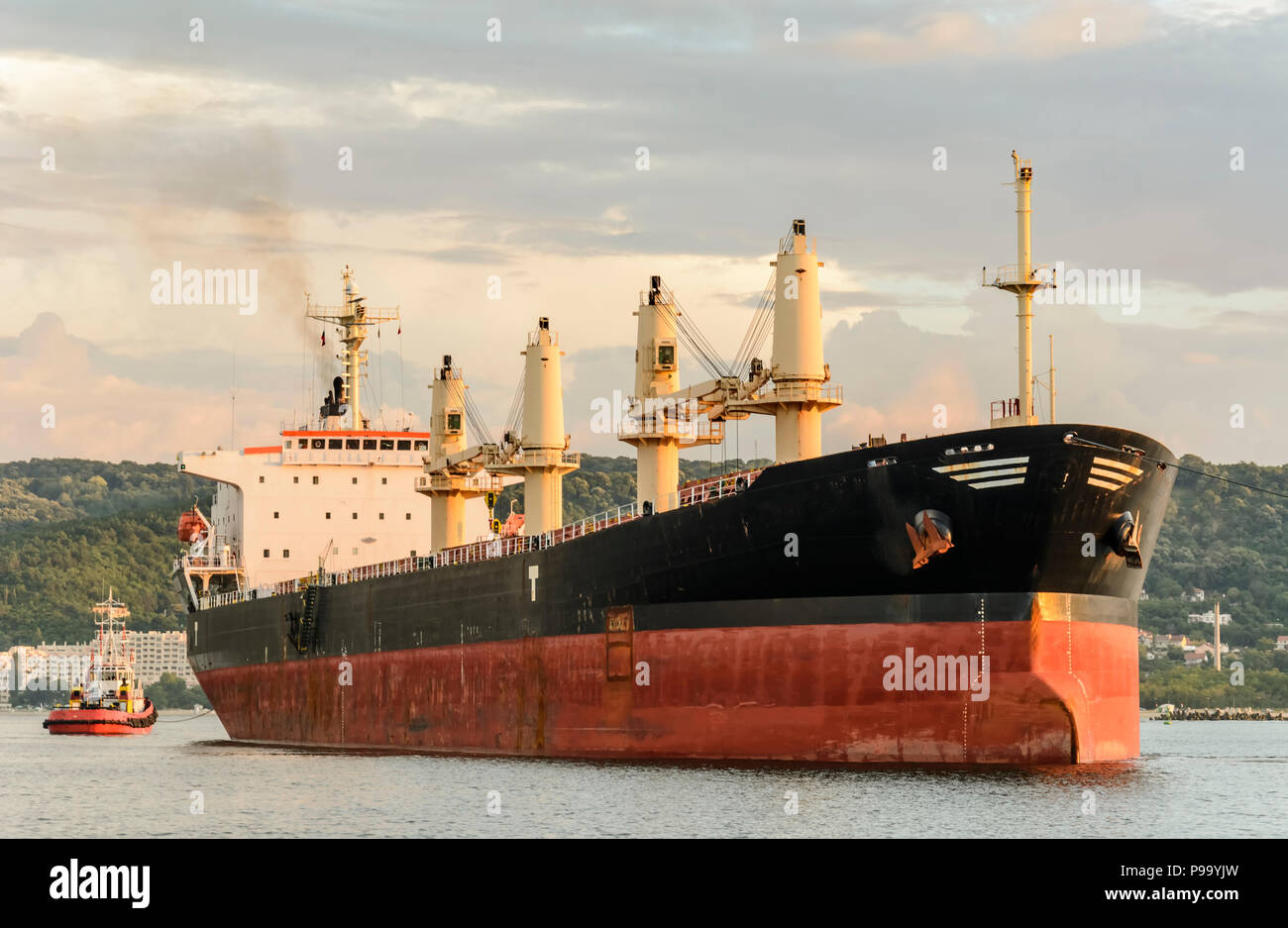 Tug boat entering the harbor with big cargo boat Stock Photo - Alamy