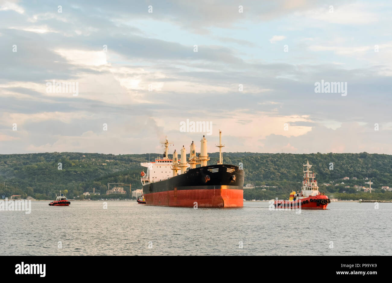 Tug boat entering the harbor with big cargo boat Stock Photo - Alamy