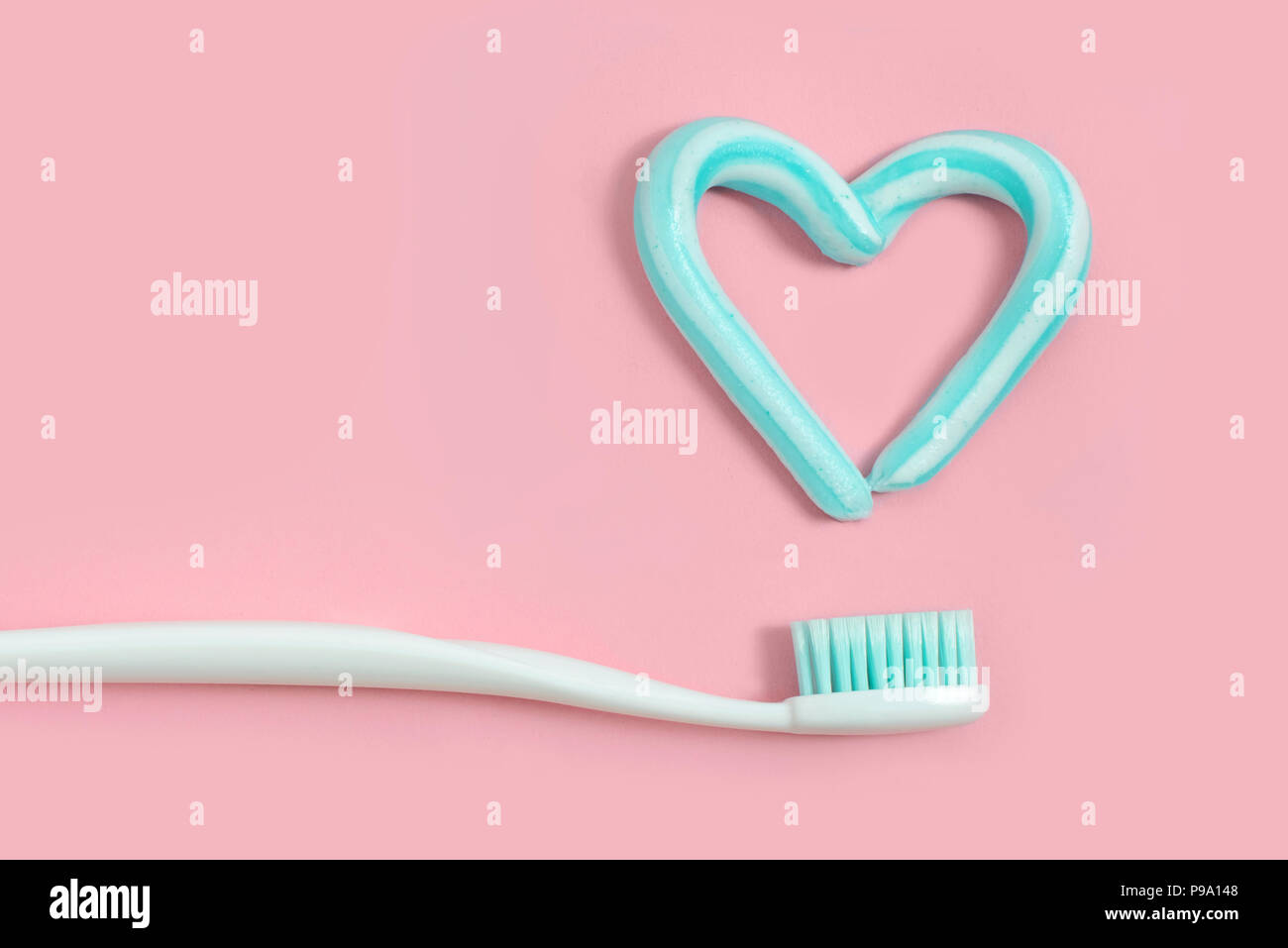 Toothbrushes and turquoise color toothpaste in shape of heart on pink ...