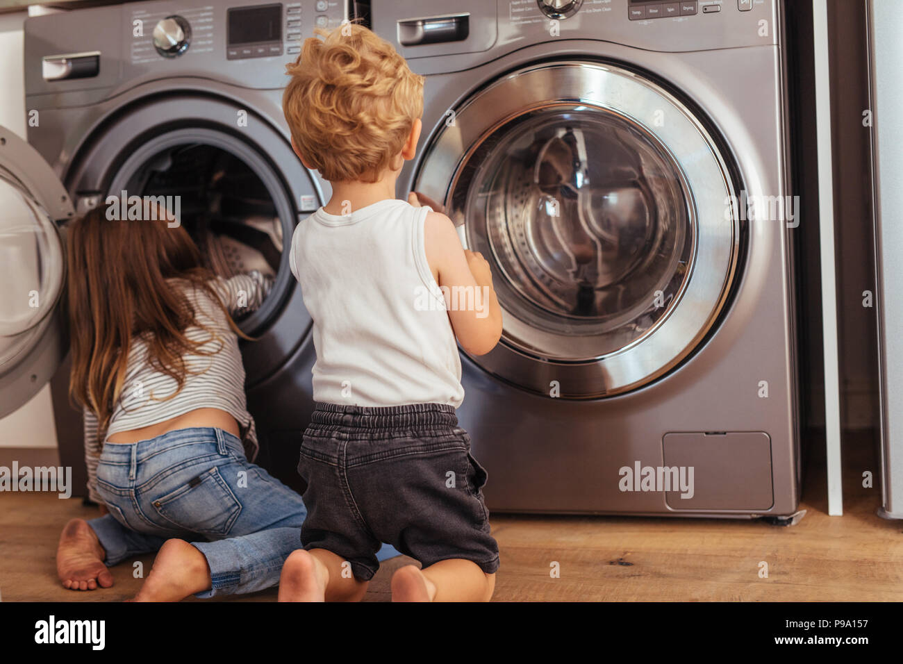 Rear view of children sitting near washing machine and playing. Kids ...