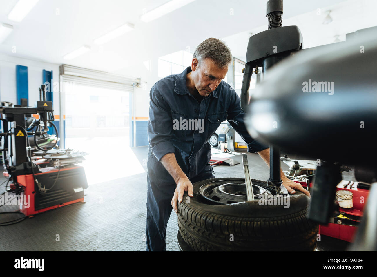 Mature man working in tire service workshop. Mechanic removing tire ...