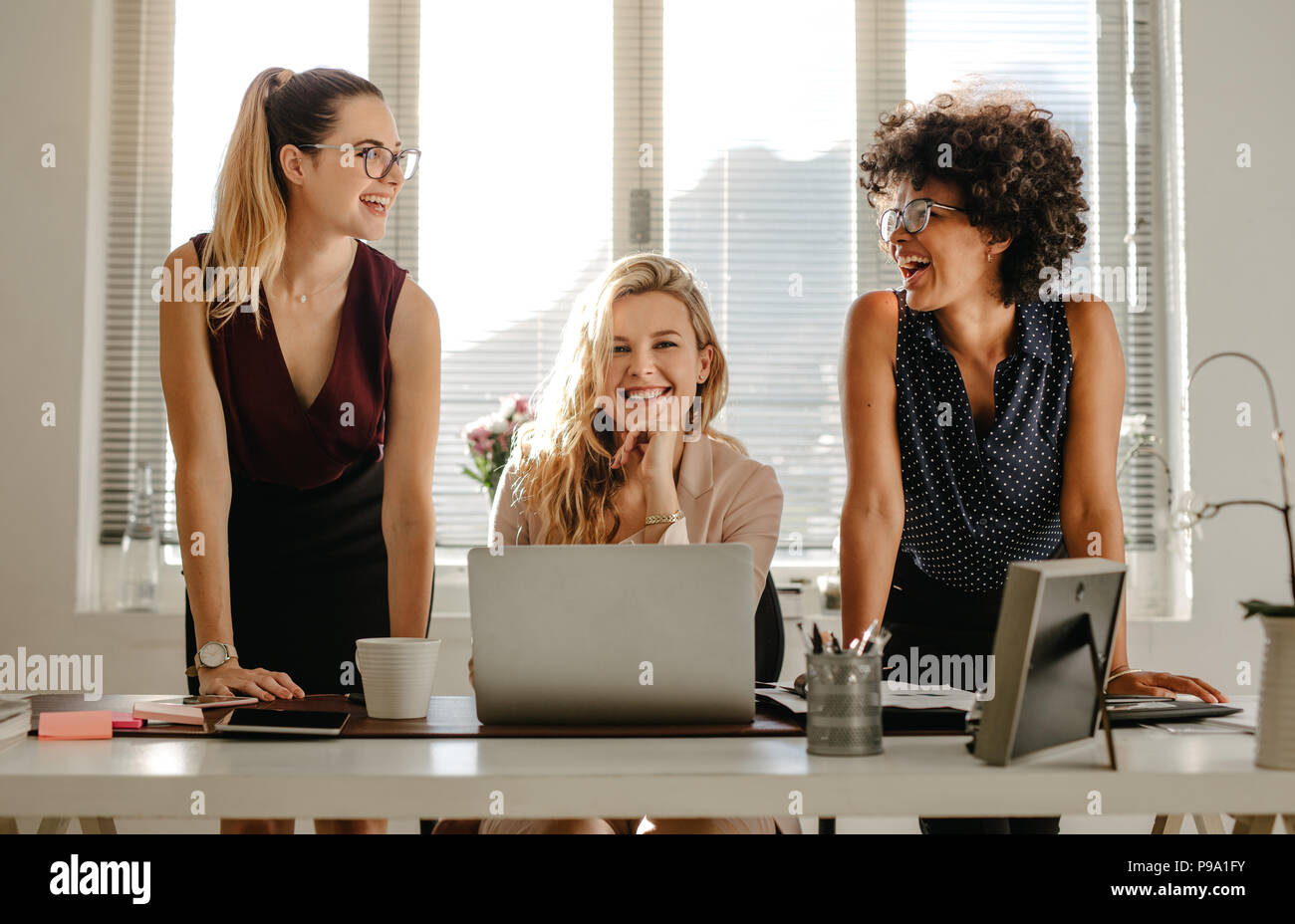 Smiling young women at work desk at office. Group of three diverse ...