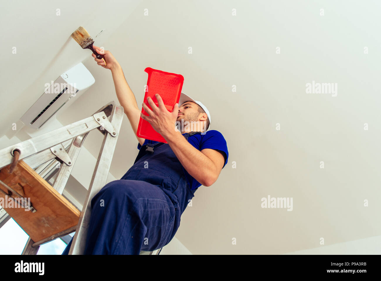 Handsome workman on ladder painting wall in white with paintbrush Stock ...