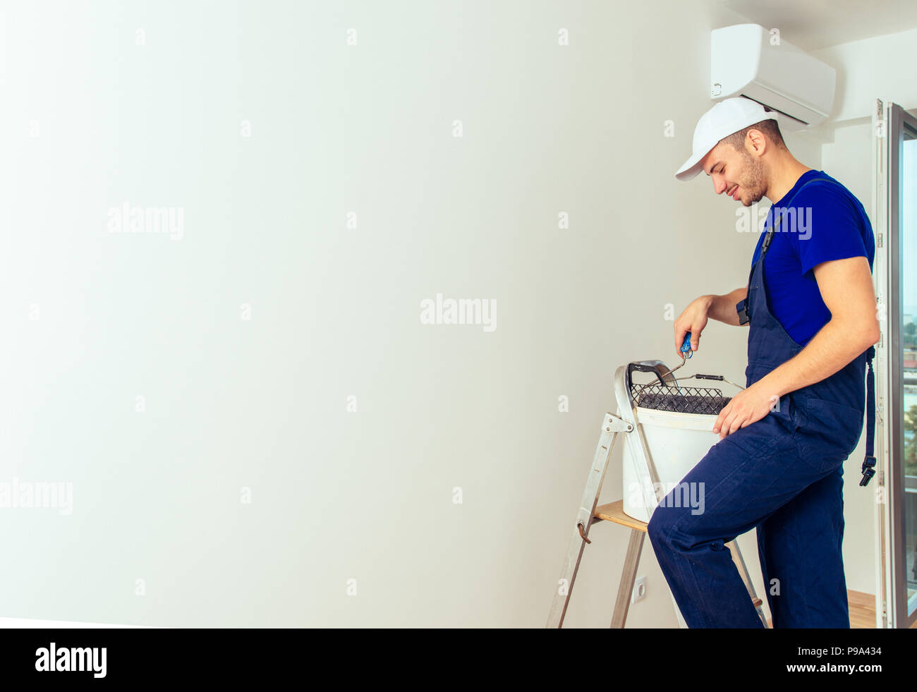 Smiling uniform guy on ladder is mixing color with paint roller Stock ...