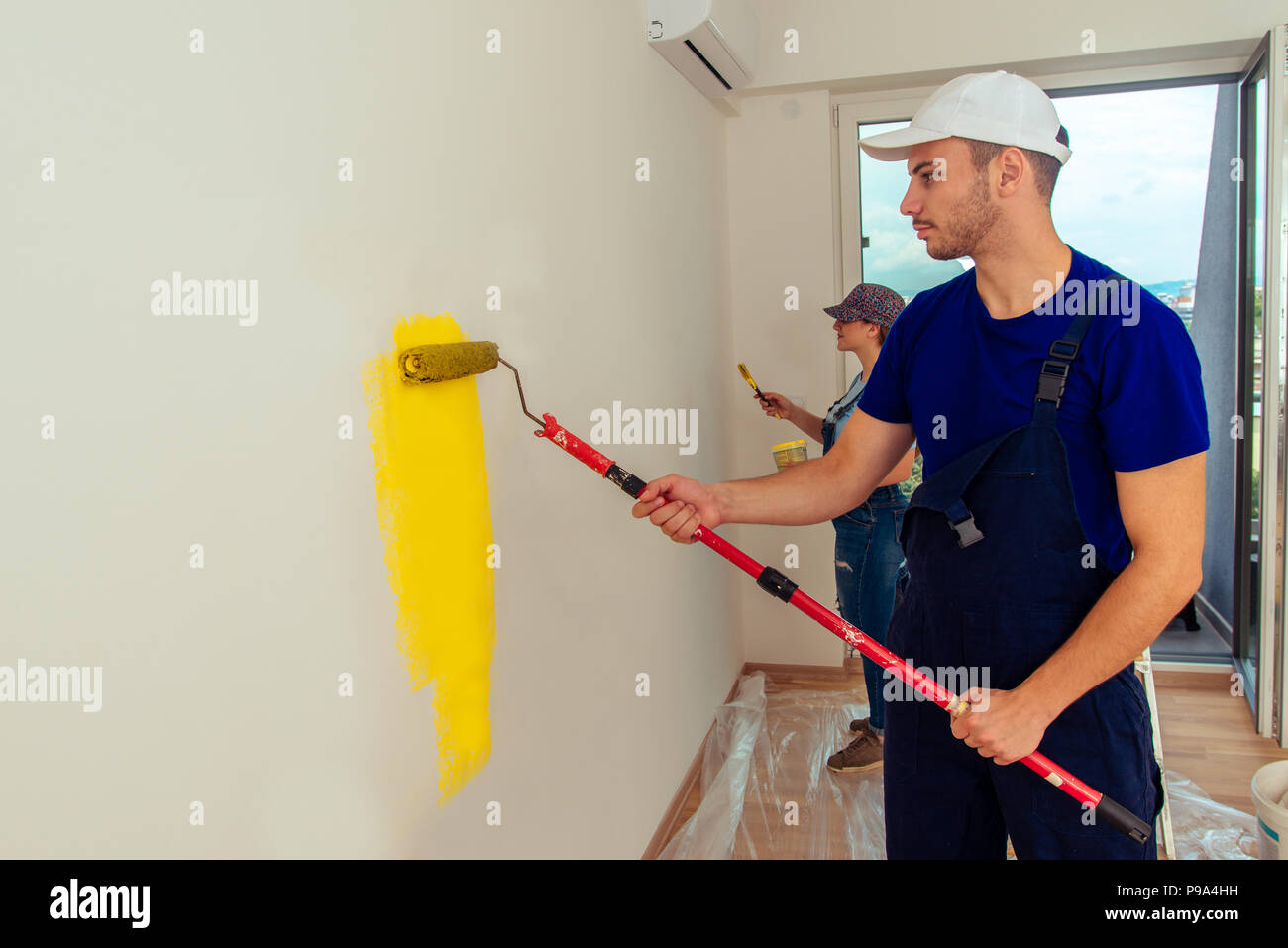 Adult guy painting room yellow with paint stick roller Stock Photo - Alamy