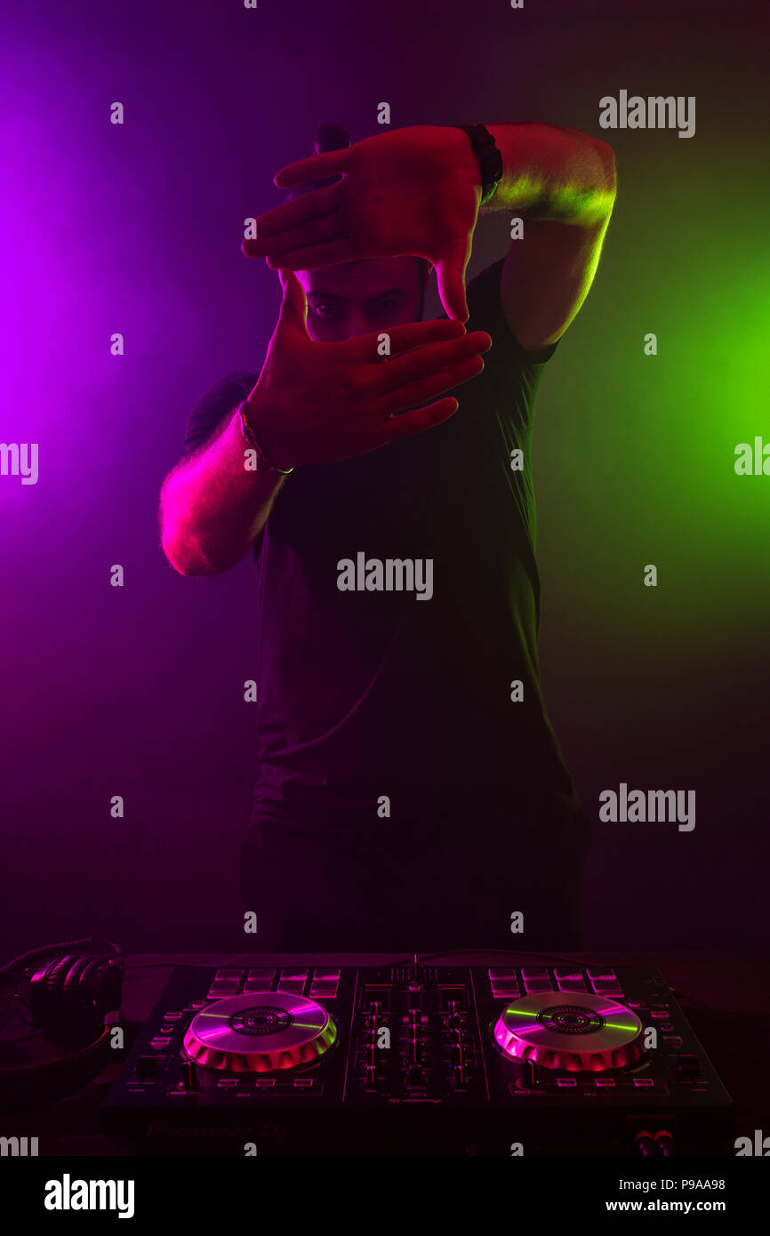 Attractive young DJ playing on turntables with color light effects ...