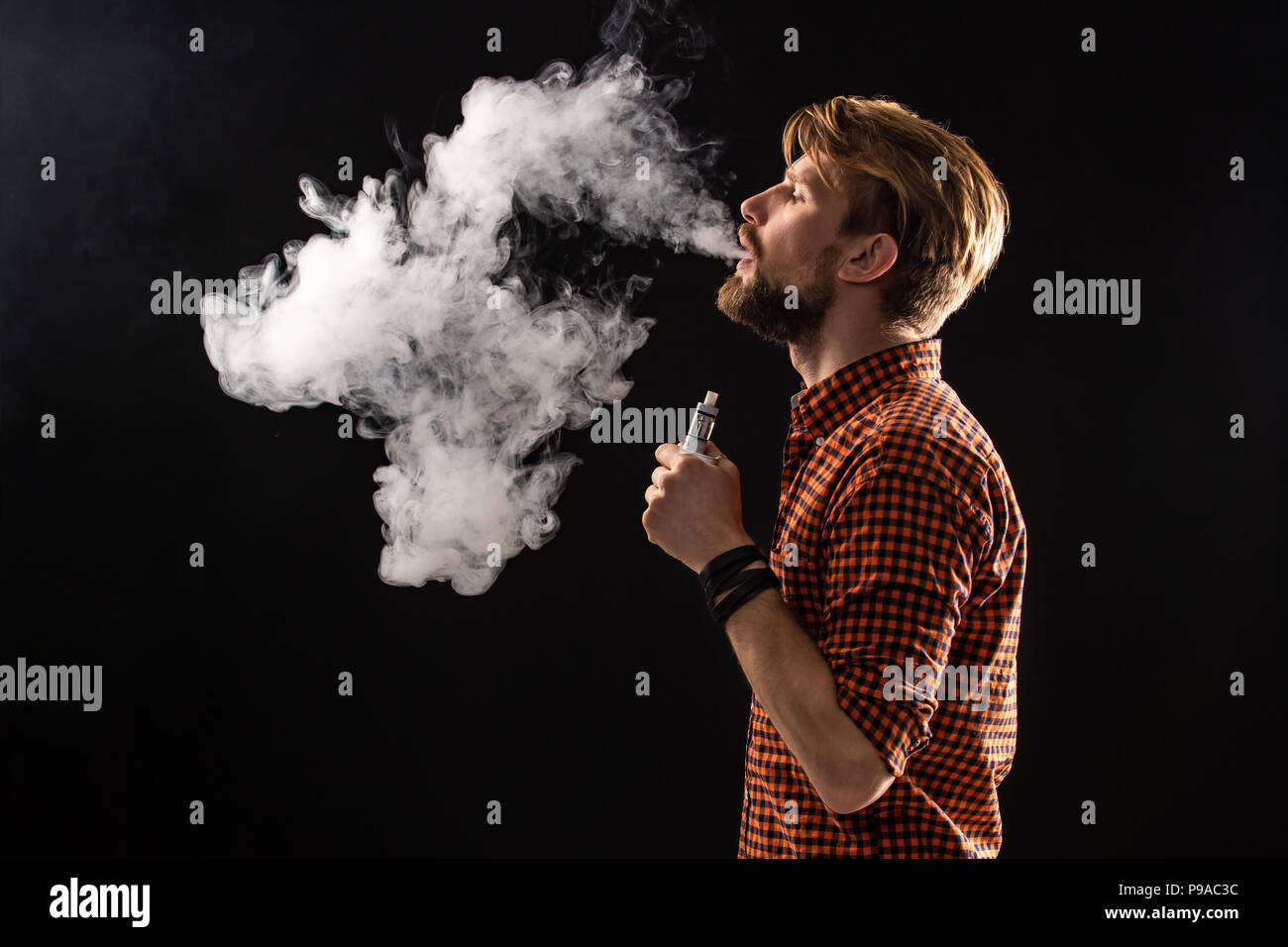 A young man with a beard and a stylish hairstyle in a shirt, smoking a ...