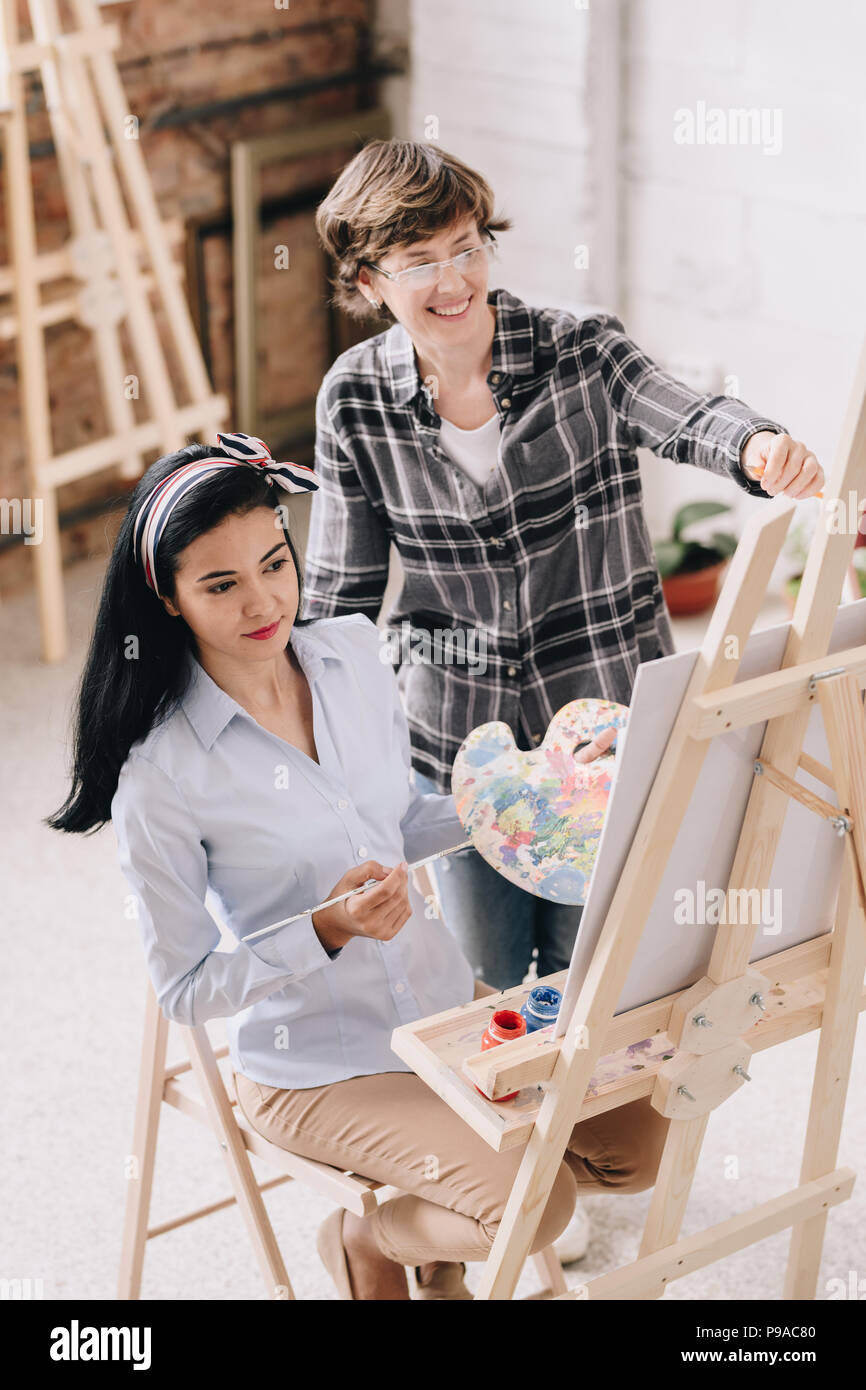 High angle portrait of smiling young woman painting sitting by easel in ...