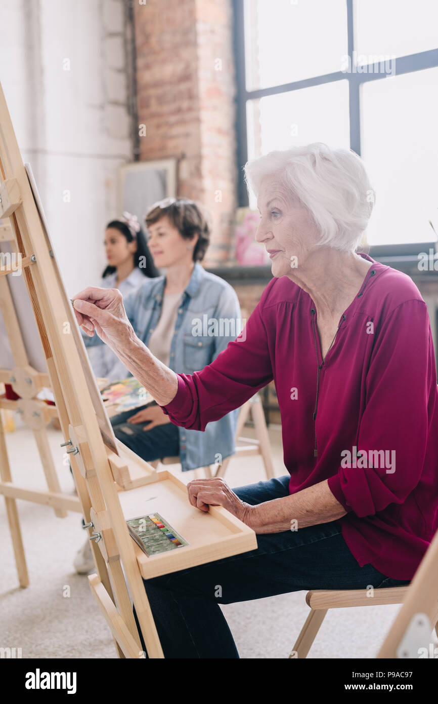 Side view portrait of art students sitting in row and painting at ...
