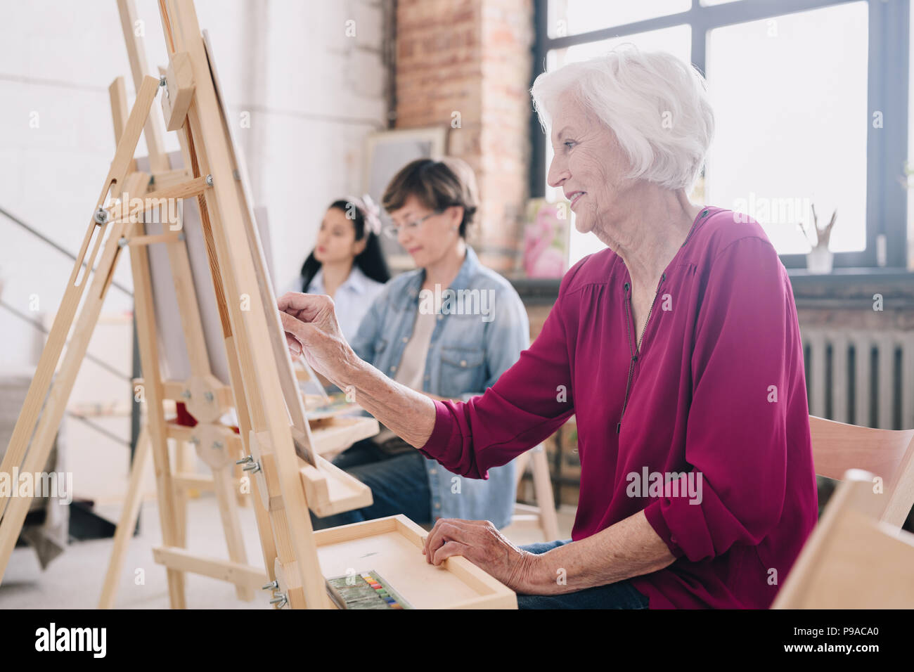 Side view portrait of art students sitting in row and painting at ...