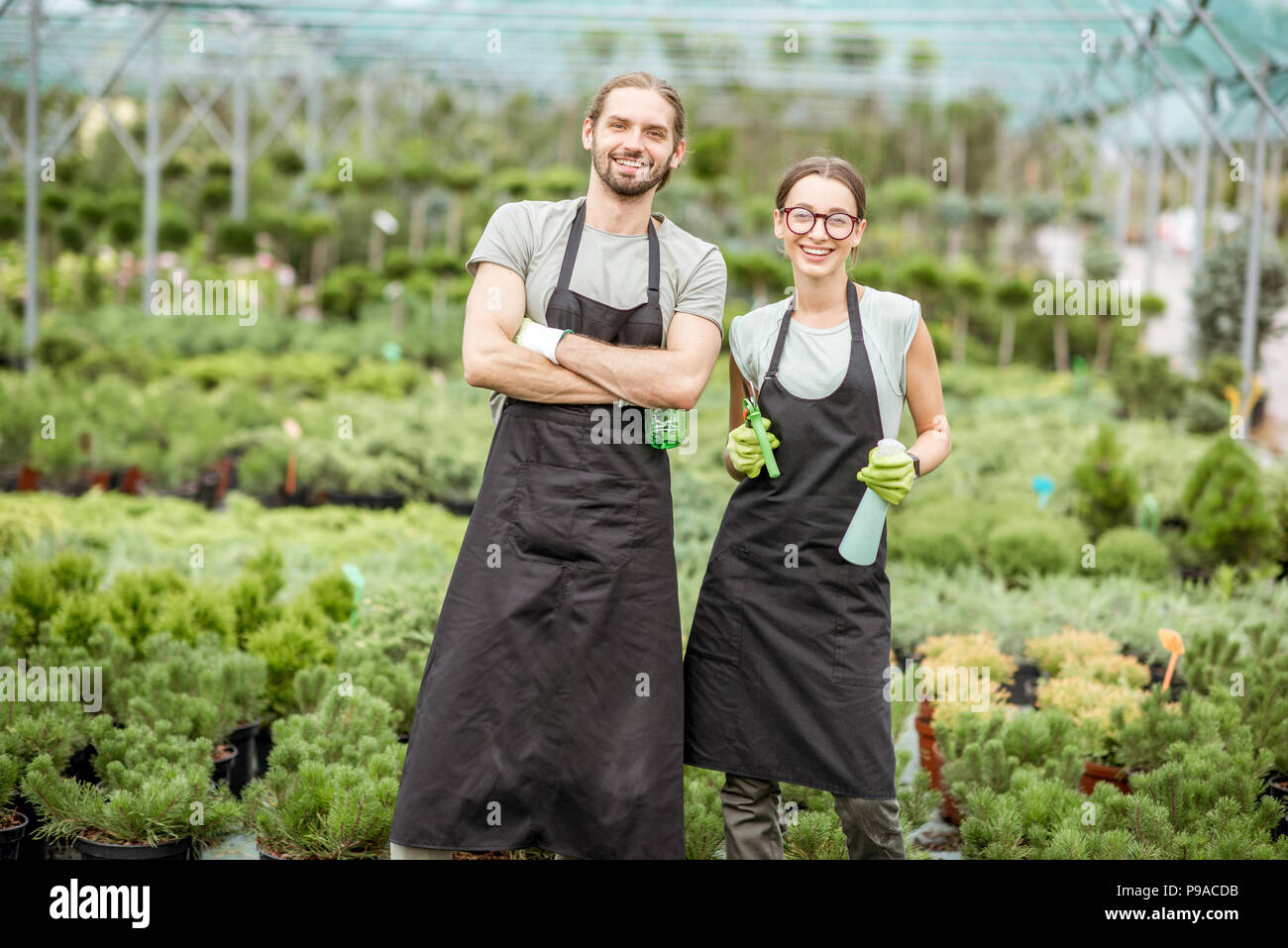 Portrait of a young couple of workers in uniform taking care of plants ...