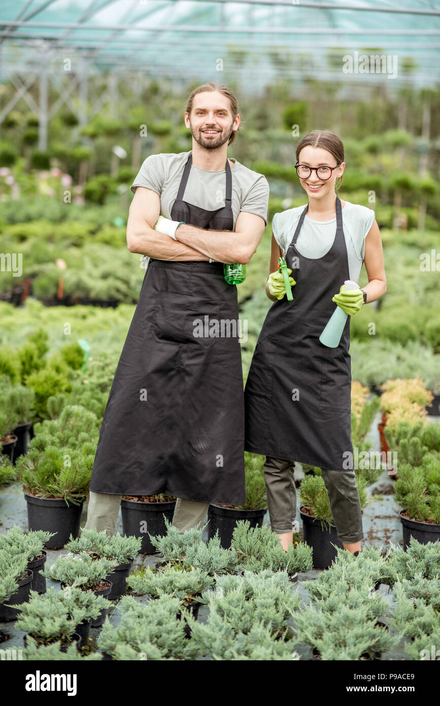 Portrait of a young couple of workers in uniform taking care of plants ...