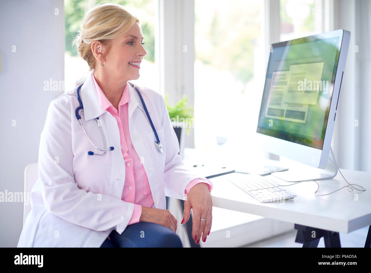 Beautiful smiling female doctor sitting in front of her computer at the ...