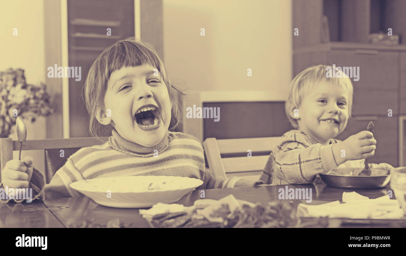 Two happy children eating food at table Stock Photo - Alamy