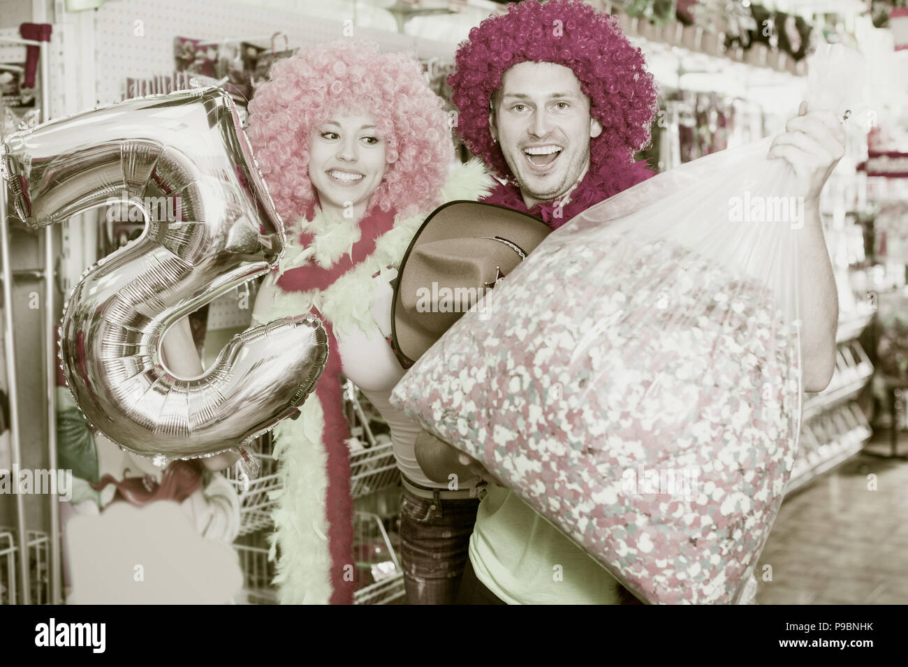 Smiling pair with big sack of confetti in store of festive things Stock ...