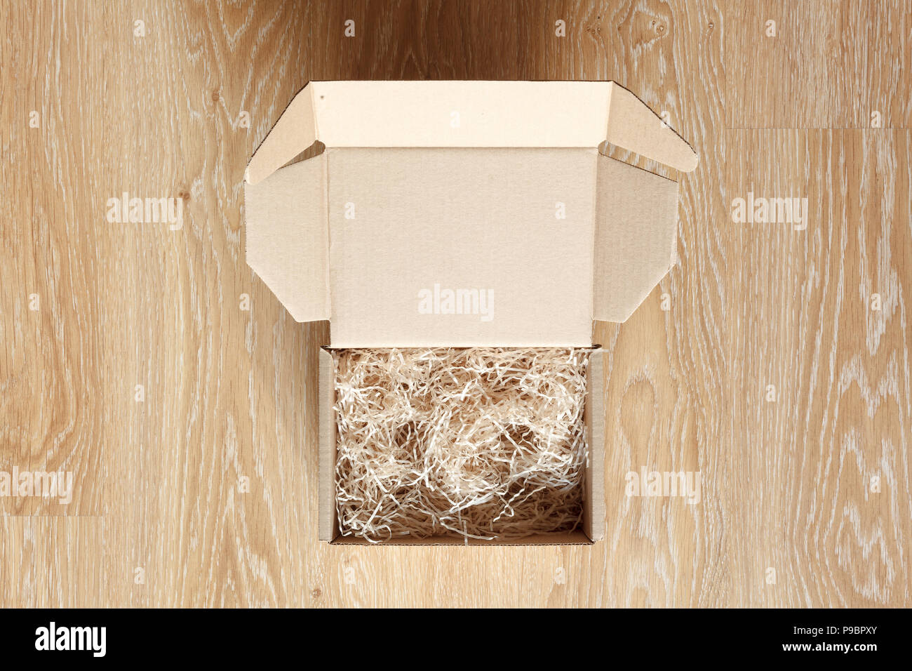 Opened cardboard box with wood excelsior shred filler on wooden ...