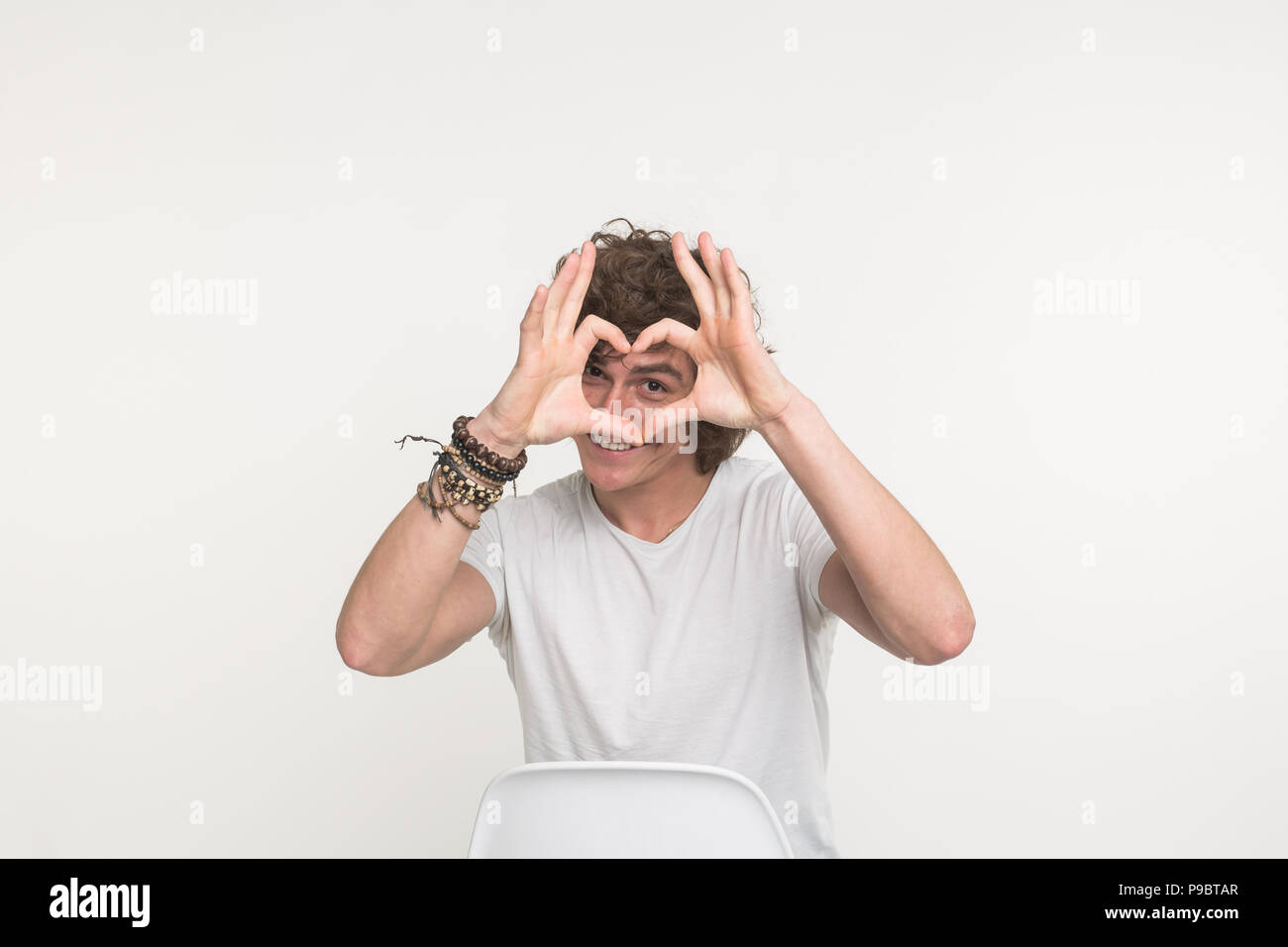Portrait of happy handsome young man making heart with fingers on white ...