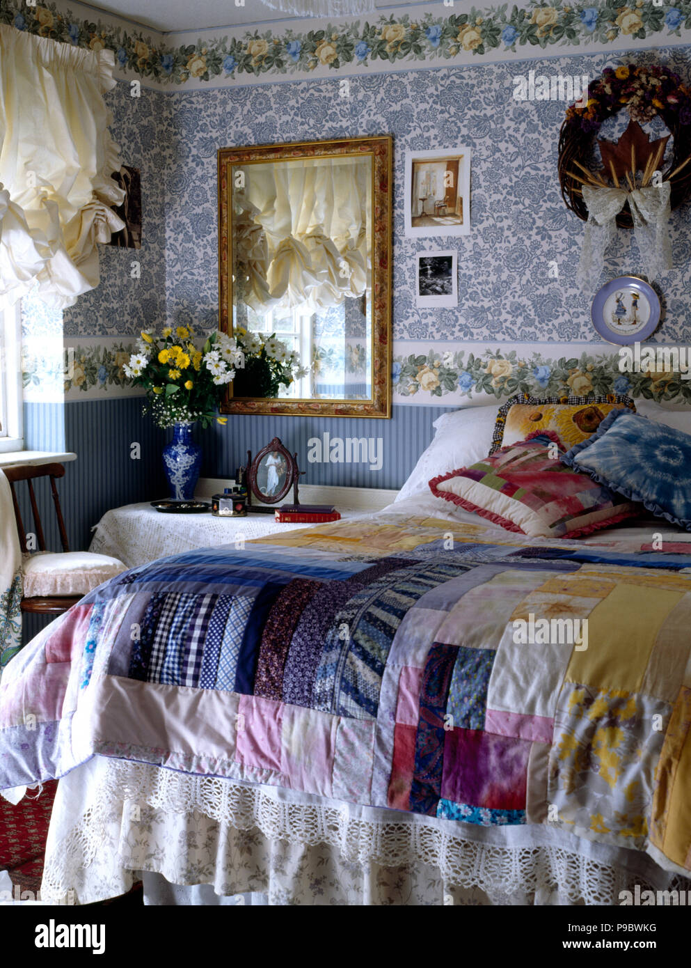 Patchwork quilt on bed in an old fashioned bedroom with blue+white ...