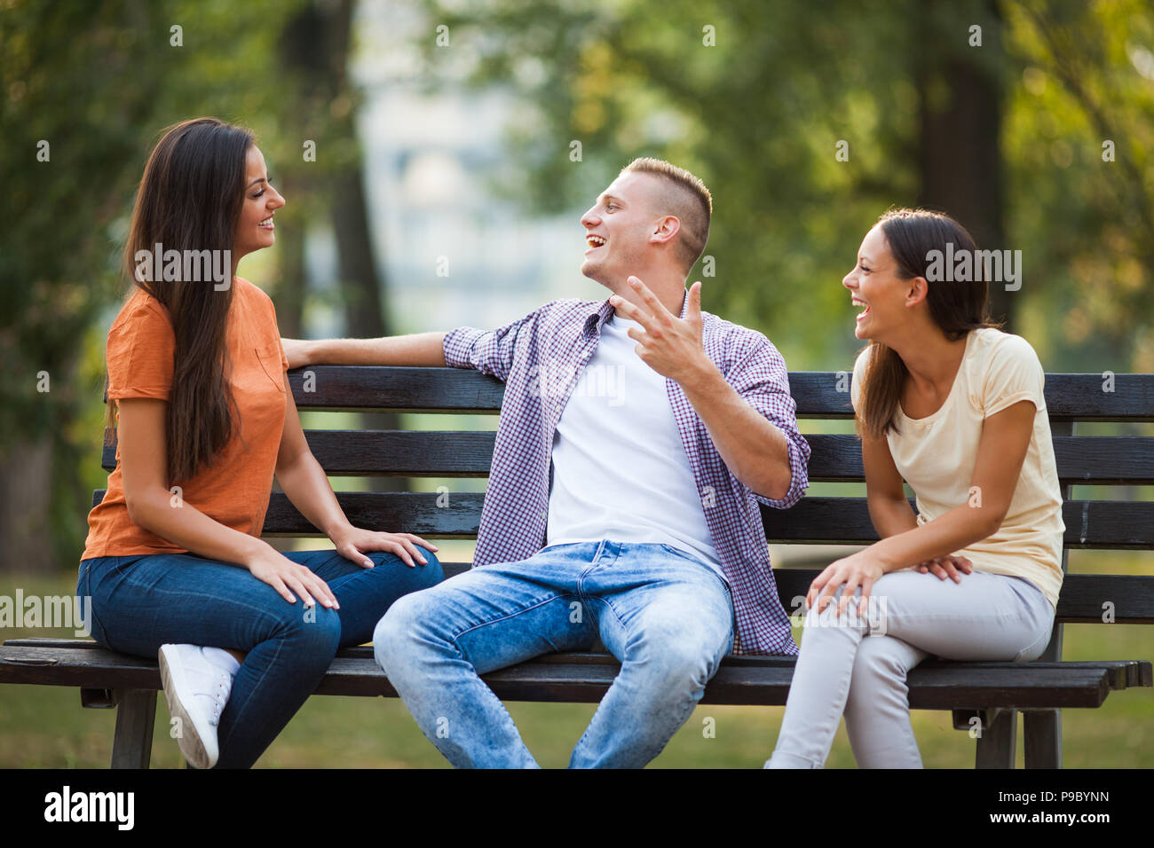 Three friends are sitting on bench in park and talking Stock Photo - Alamy