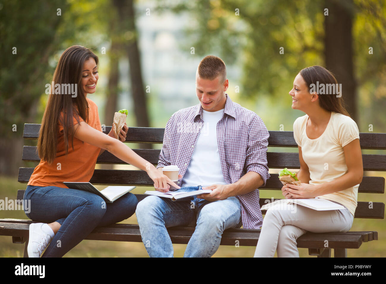 Three students are sitting on bench in park and learning Stock Photo ...