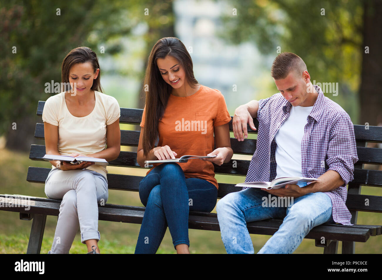 Three students are sitting on bench in park and learning Stock Photo ...