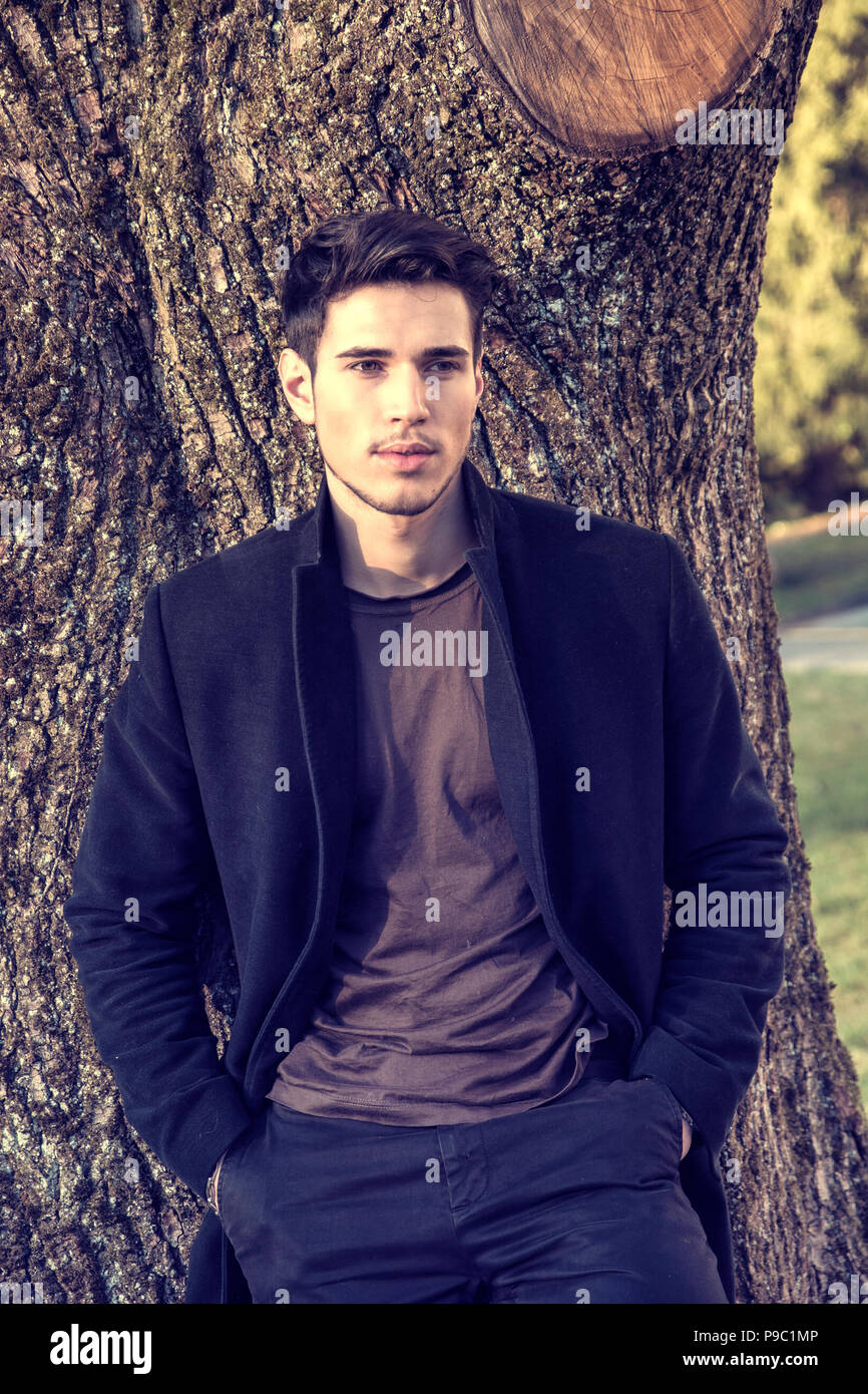 Handsome young man leaning against tree Stock Photo - Alamy