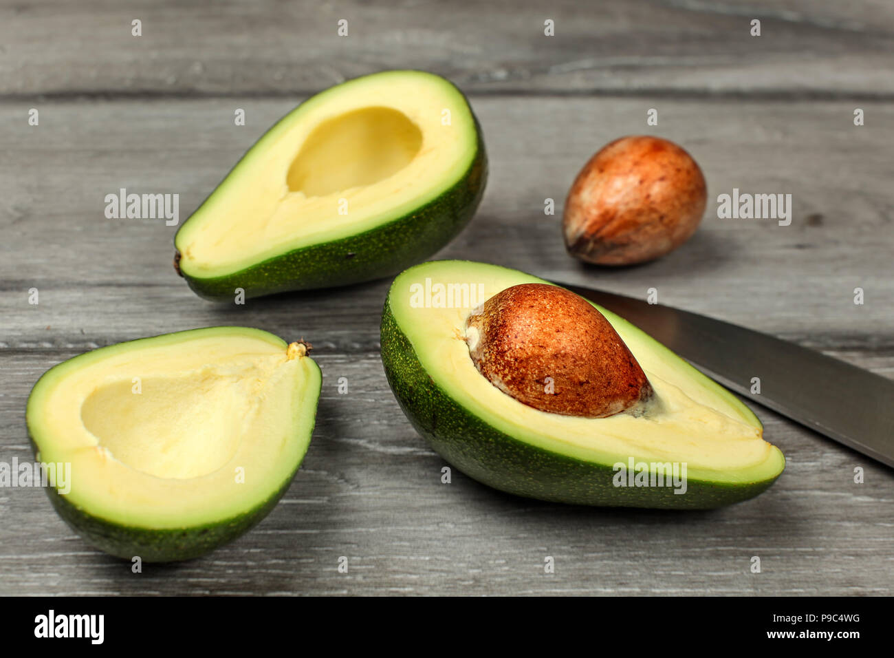 Avocado, cut in half, two seeds and chefs knife on gray wood desk Stock ...