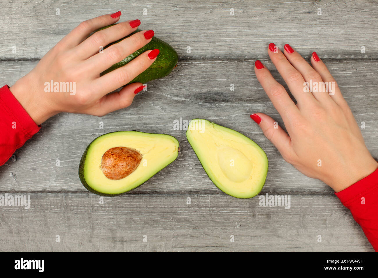 Table top view - woman hands, and avocado cut in half on gray wood desk ...