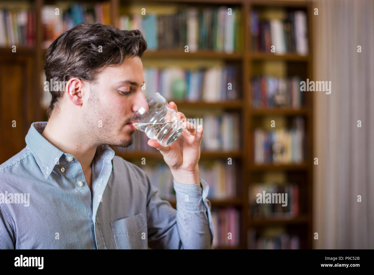 Casual man drinking water in library Stock Photo - Alamy