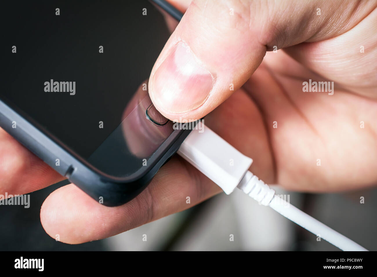 Using A Black Mobile Phone, Connected To A White USB Cable, Holded By A ...