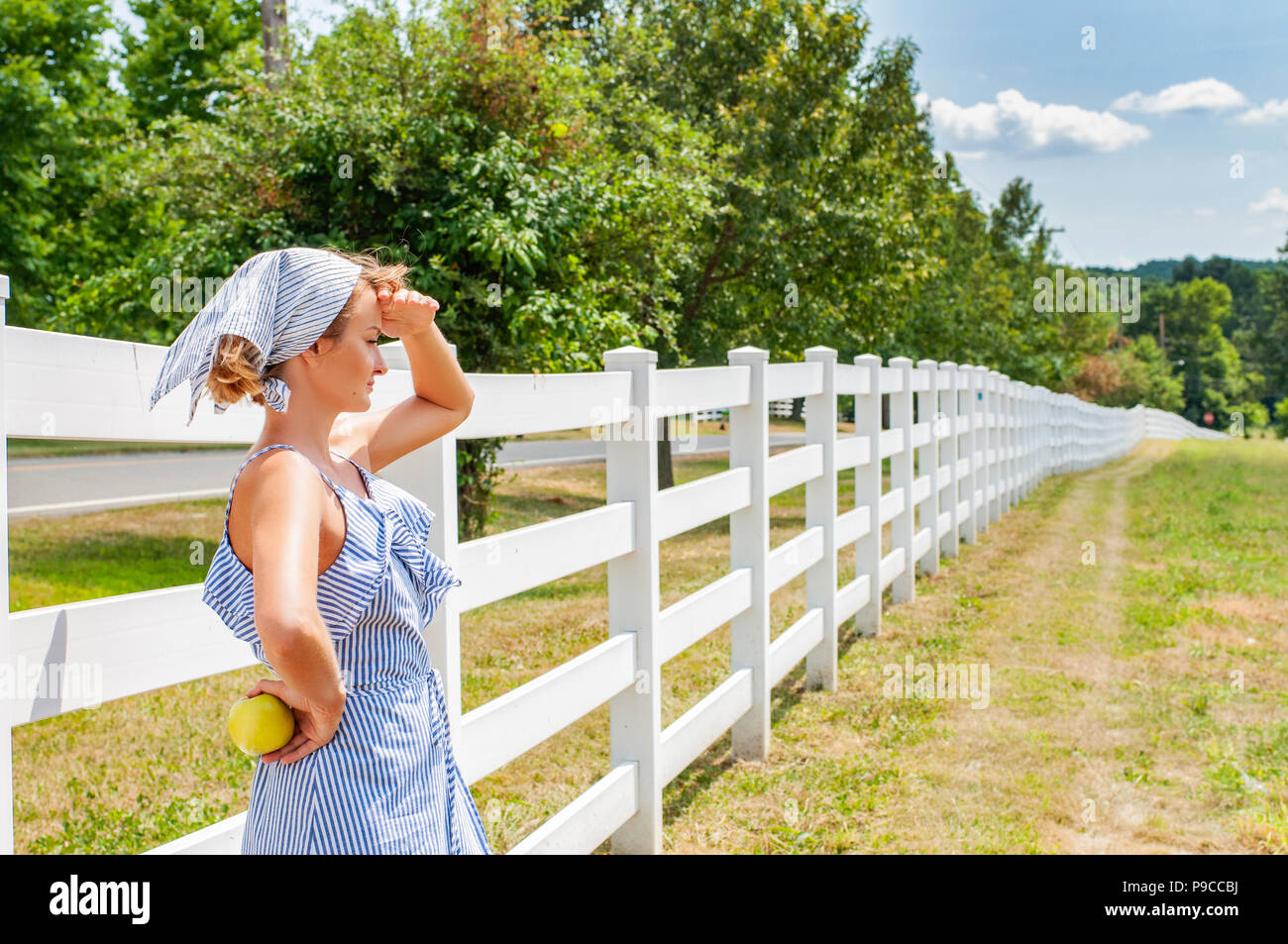 Farm. Pretty woman standing near fence on countryside and enjoying ...