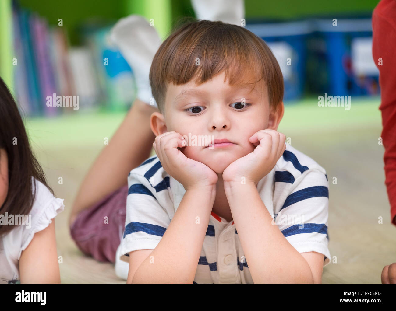 Boy kid lay down on library floor with bored feeling in preschool ...