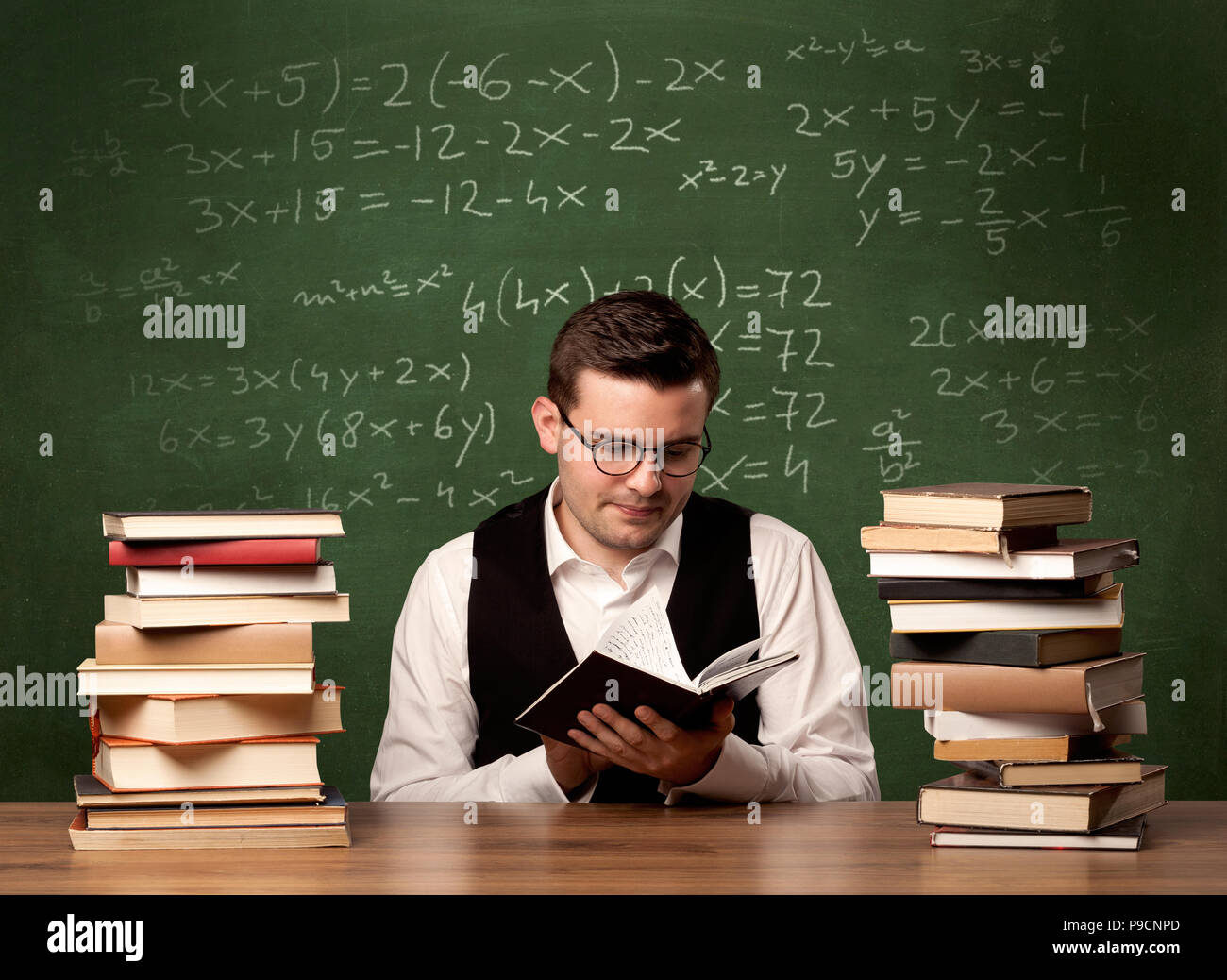 A young ambitious teacher in glasses sitting at classroom desk with ...