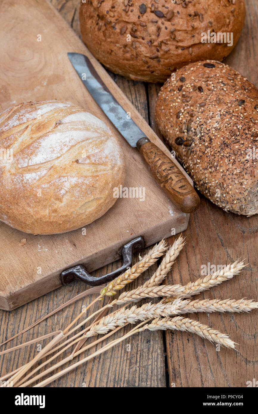 White bread and seeded loaves on a bread board with wheat and a bread ...