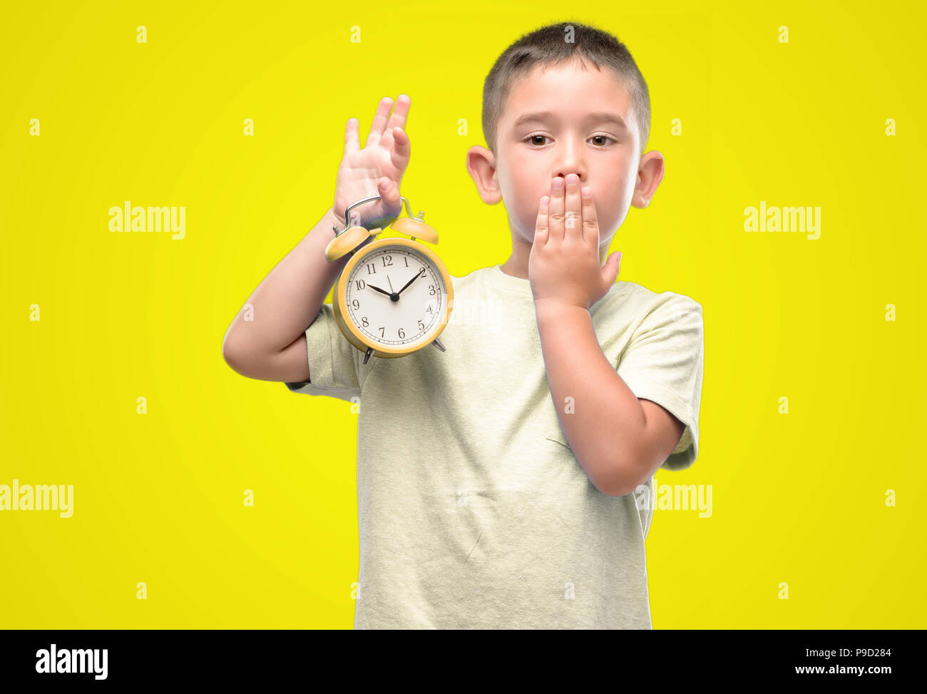 Little child holding alarm clock cover mouth with hand shocked with ...