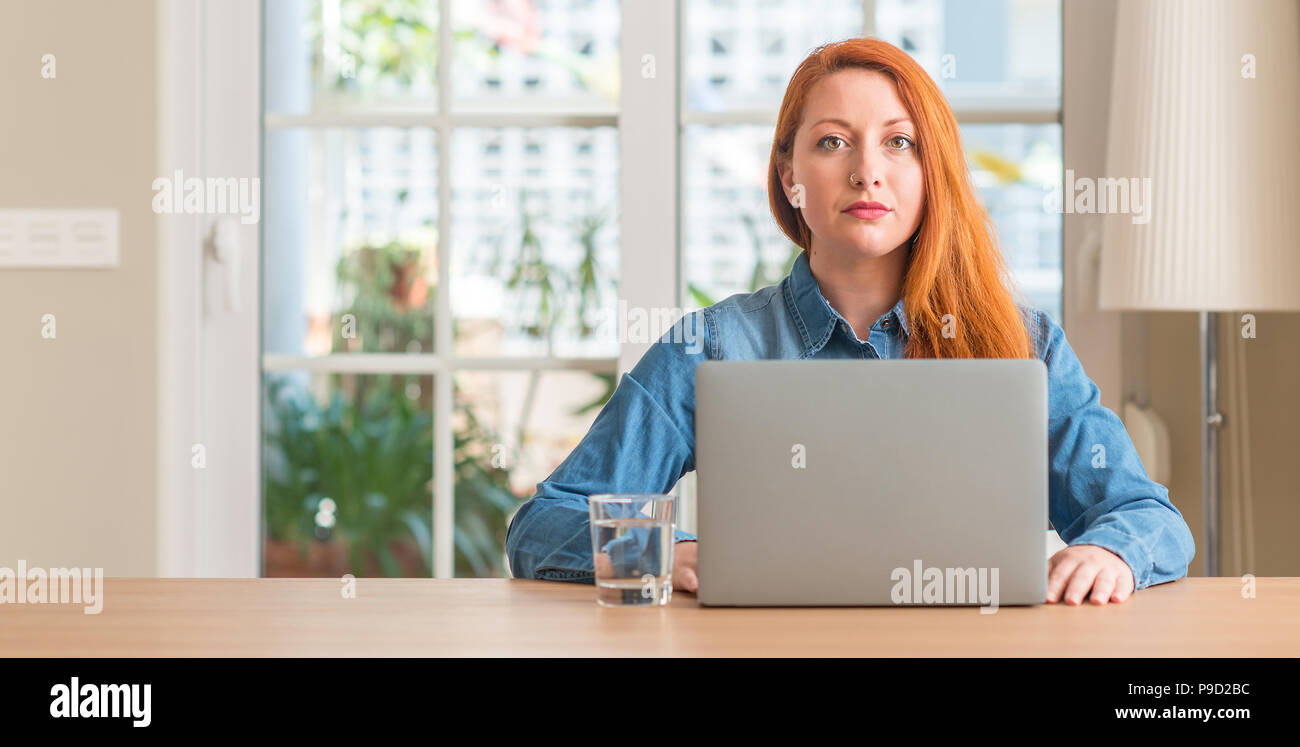 Redhead woman using computer laptop at home with a confident expression ...