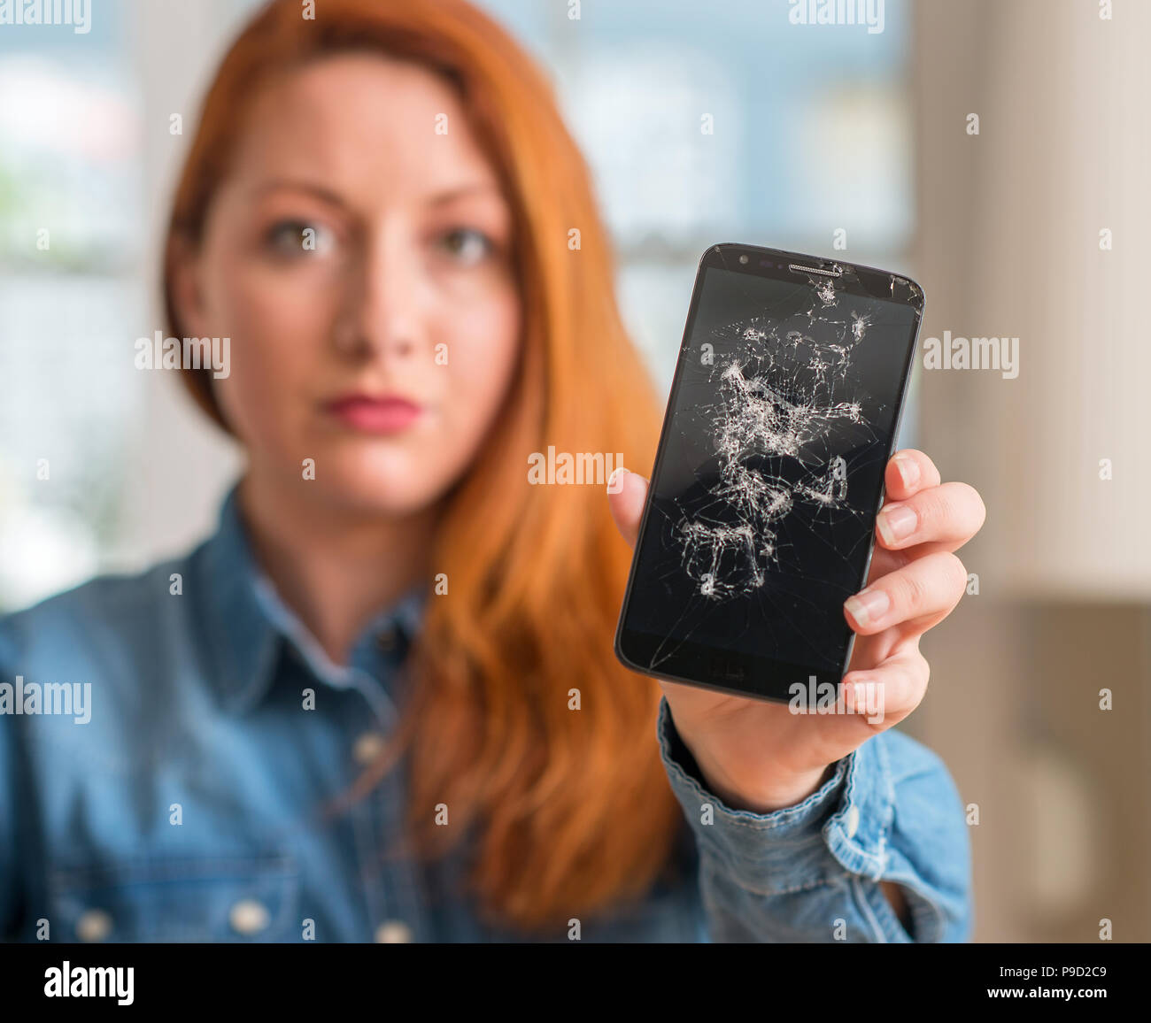 Redhead woman holding broken smartphone with a confident expression on ...