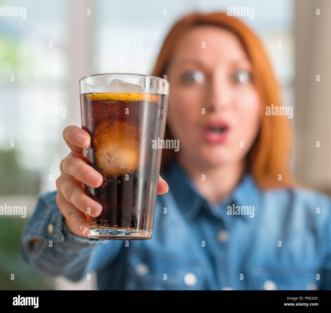 Redhead woman holding soda refreshment scared in shock with a surprise ...