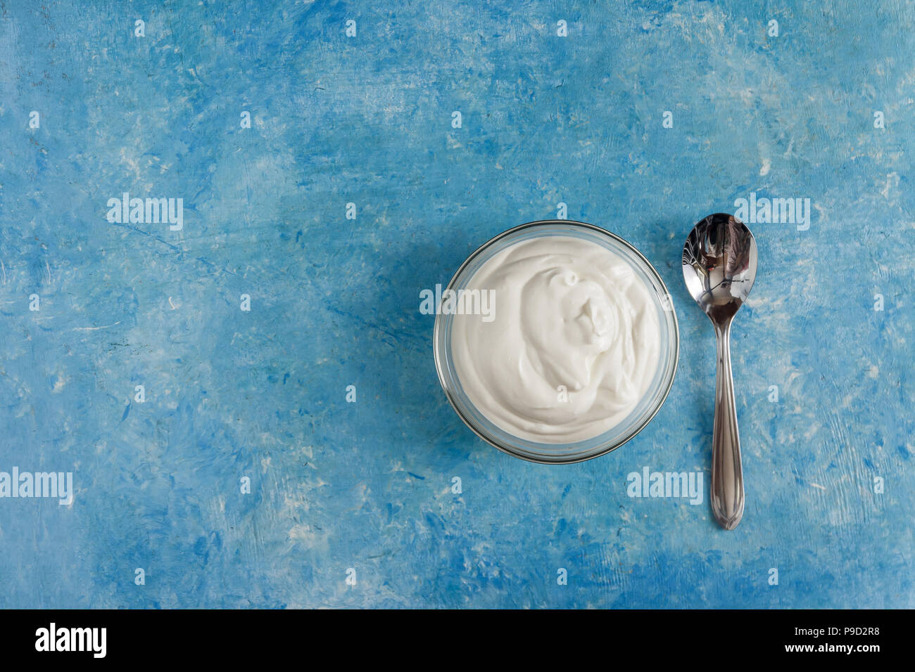 Greek yogurt in a bowl with a spoon, close-up on blue stone table top ...
