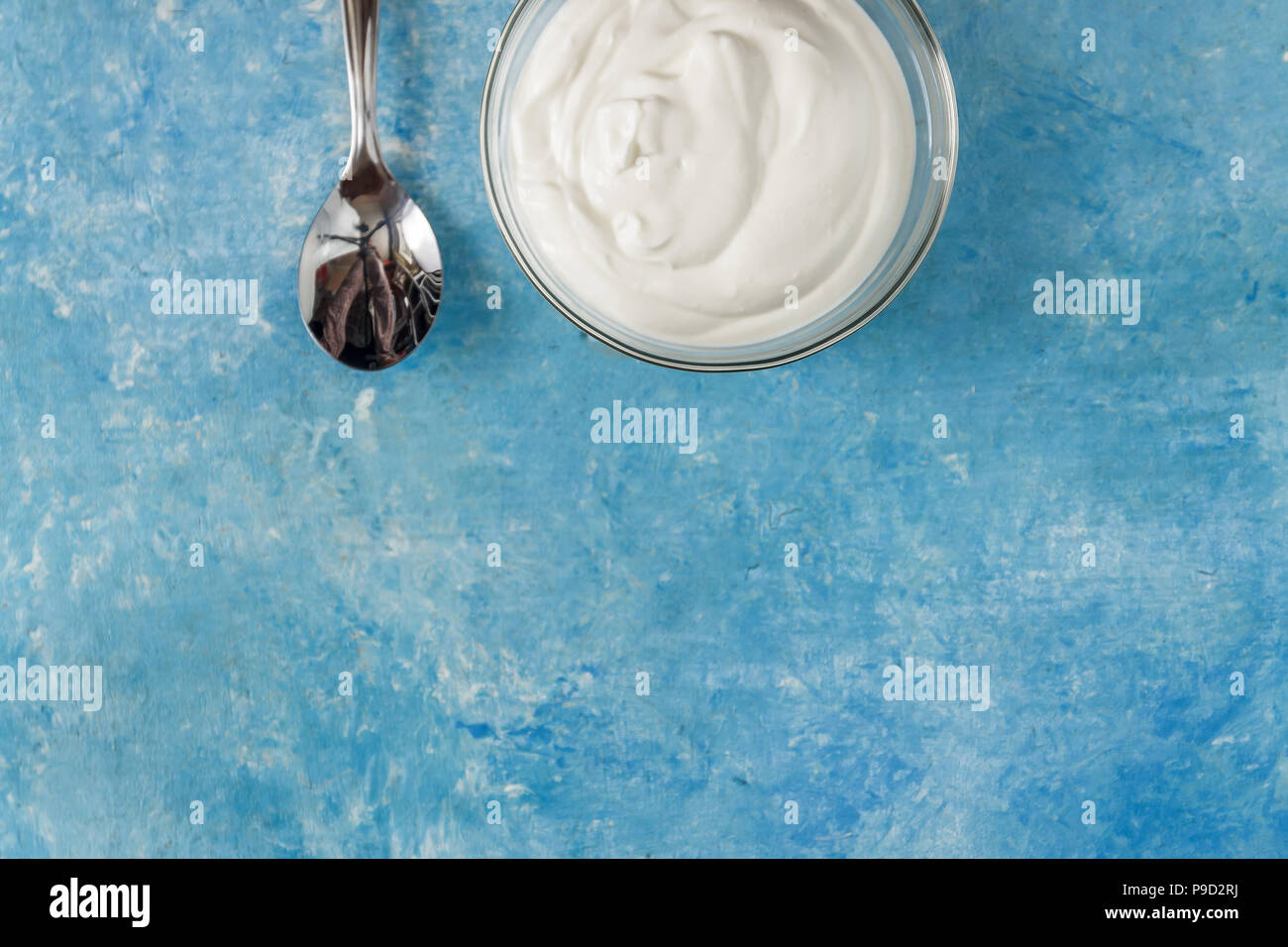 Greek yogurt in a bowl with a spoon, close-up on blue stone table top ...