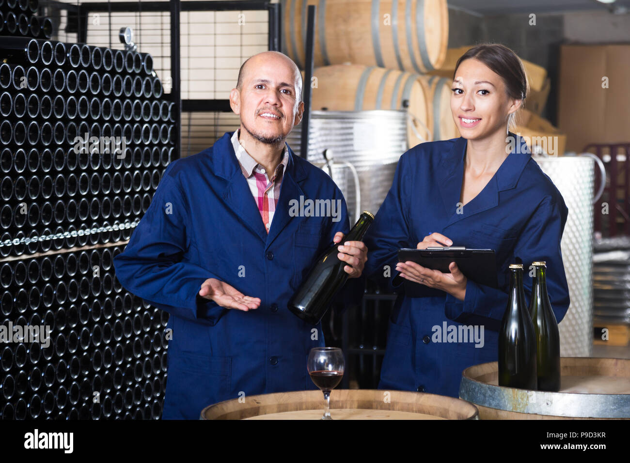 Woman with cardboard standing with male worker in small winery cellar ...