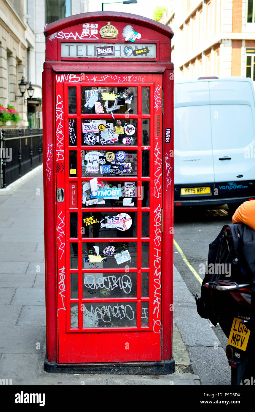 Traditional red telephone box covered in graffiti and stickers, central ...